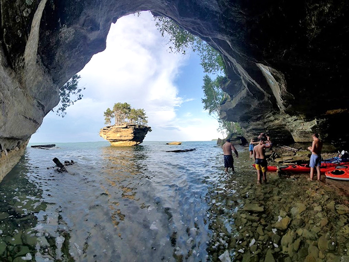 From inside a shoreline cave, Turnip Rock appears framed like a painting – nature's perfect composition of water, stone, and resilient greenery.
