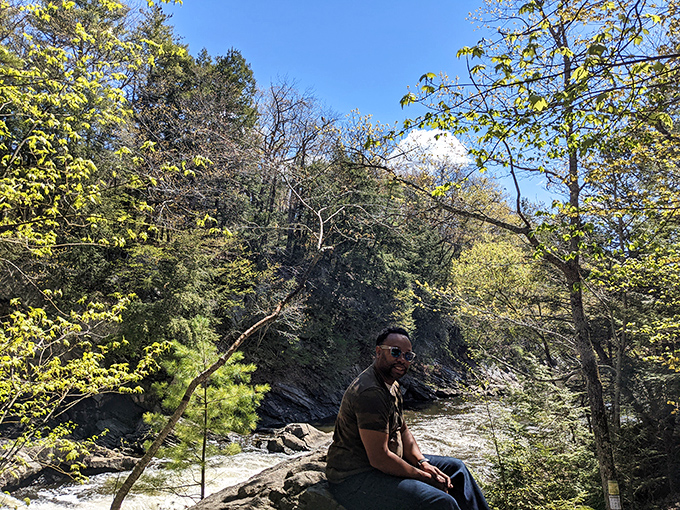 A visitor enjoys a moment of tranquility perched on rocks overlooking the flowing river below.
