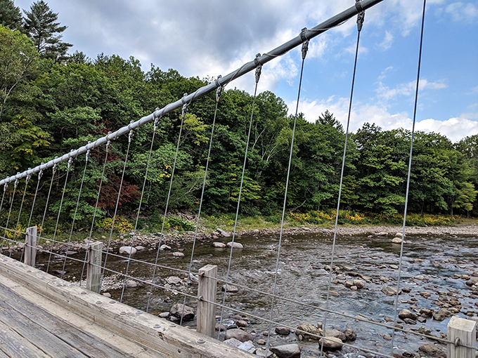The Carrabassett River flows gently beneath the historic structure, its rocky bed visible through crystal clear Maine waters.