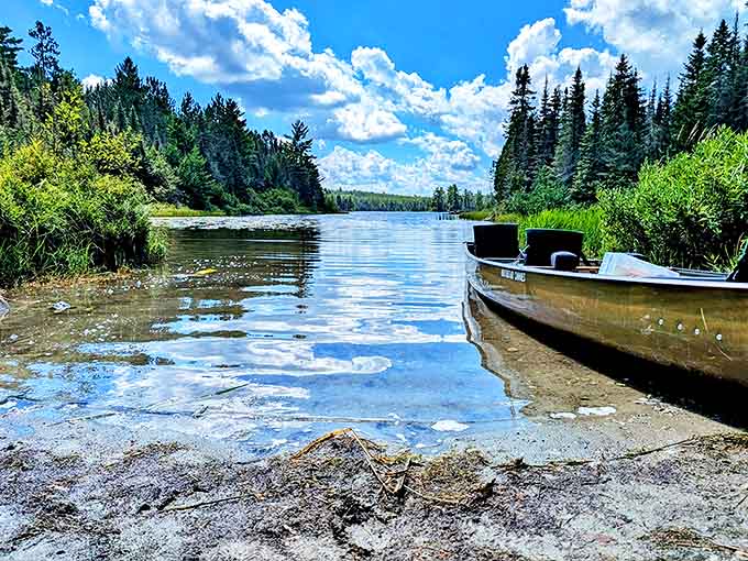 Boundary Waters' pristine lakes mirror perfect blue skies and fluffy clouds, with a lone canoe ready for wilderness adventures.