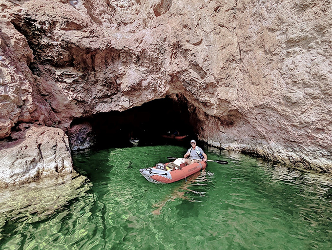 A small boat glides through the emerald waters of this hidden cave, where sunlight creates an otherworldly green glow against the rock walls.