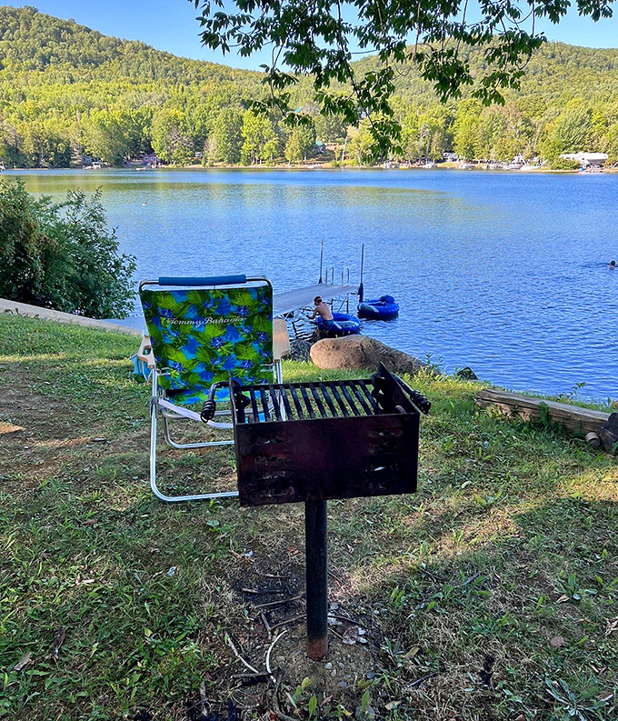 A serene view of Rangeley Lake with mountains in the background and a simple grill and chair setup perfect for lakeside relaxation.
