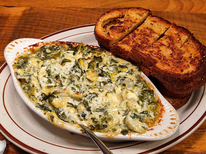 The spinach artichoke dip bubbles with molten cheese goodness, ready to transform ordinary bread into vehicles of creamy delight.
