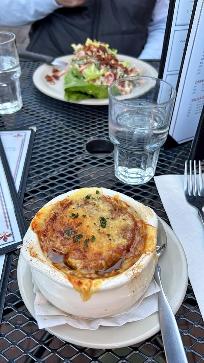 French onion soup crowned with melted cheese stretches like edible gold, hiding depths of rich broth that justify every three-hour French lunch ever taken.