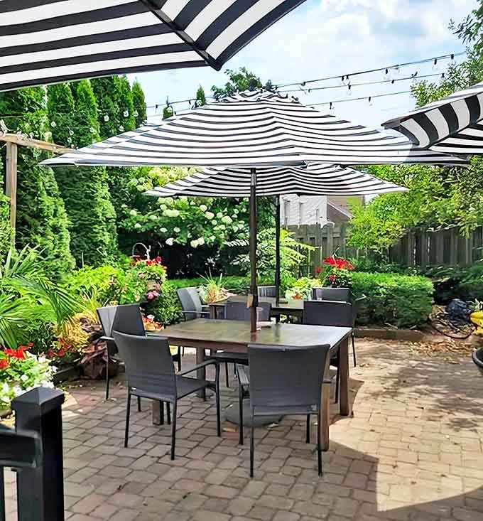 The garden patio offers a leafy retreat where striped umbrellas and lush greenery create the perfect summer dining sanctuary.
