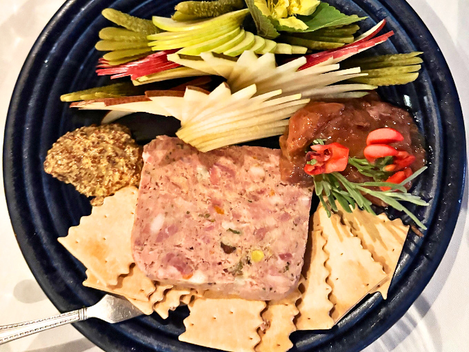 Country p&acirc;t&eacute; served with all the traditional accompaniments &ndash; cornichons, mustard, and crackers arranged on a blue plate like a rustic still life.