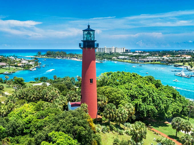 Jupiter Inlet Lighthouse's vibrant red tower creates a stunning contrast against turquoise waters and lush greenery. A Florida icon since 1860.