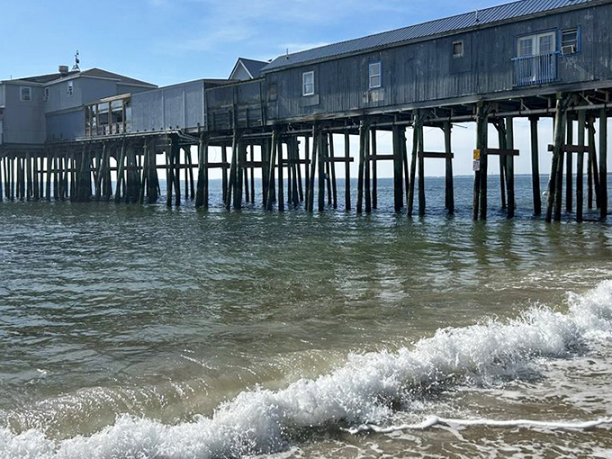 The iconic Old Orchard Beach pier extending into the Atlantic Ocean, with waves crashing beneath its wooden structure on a perfect summer day.