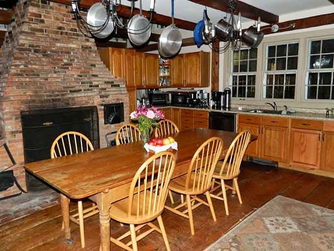 Exposed beams and a brick fireplace create an authentic colonial atmosphere in this beautifully preserved historic kitchen space.