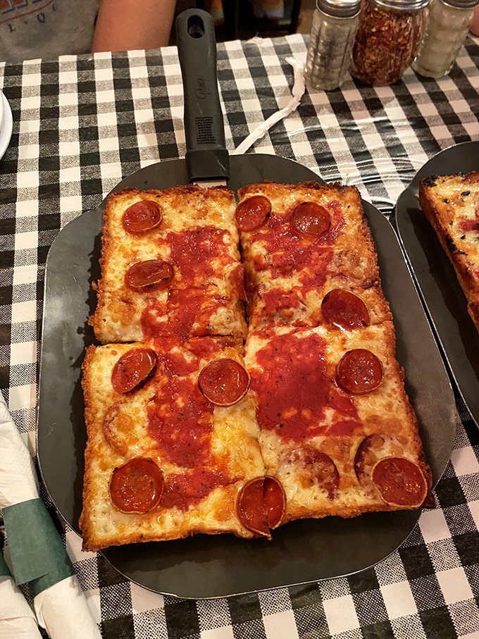 Detroit-style pepperoni pizza in its natural habitat &ndash; crispy-edged, square-cut perfection that makes round pizzas seem like they're missing corners.