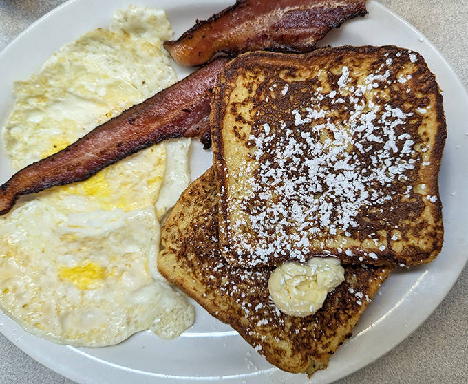 Morning perfection on a plate &ndash; golden French toast dusted with powdered sugar alongside eggs and bacon cooked to precise specifications.