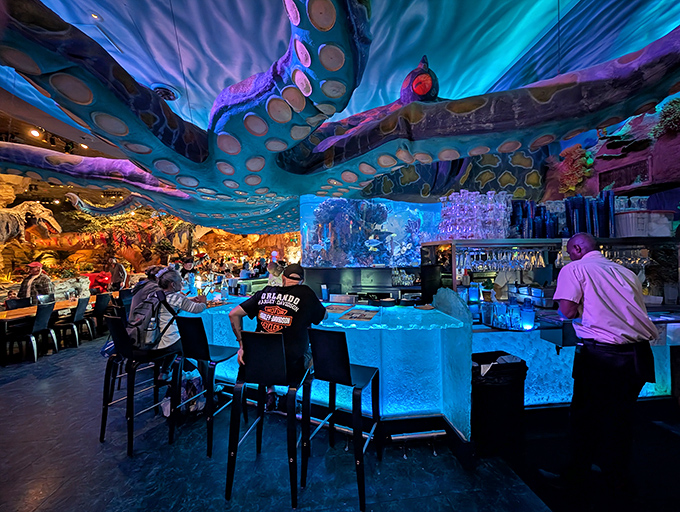 The oceanic bar glows with blue light beneath tentacles, serving up themed cocktails with names like "Primitive Punch" in souvenir glasses worth taking home.