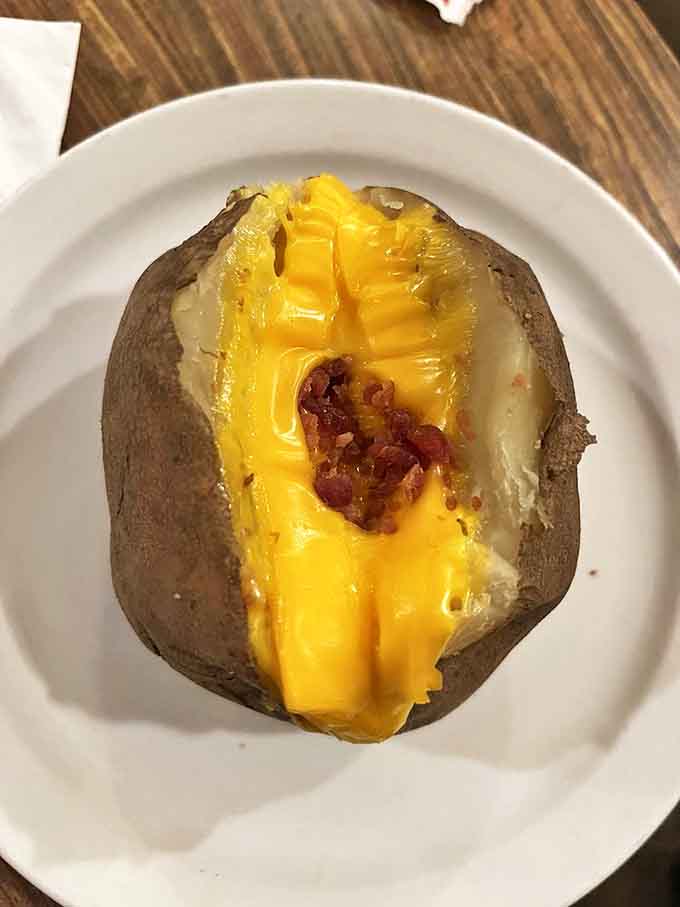 A loaded baked potato that's dressed for success &ndash; cheese, bacon, and butter creating a trifecta of comfort food perfection.
