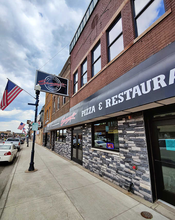 Sammy's Pizza's classic storefront with stone accents and American flags creates a welcoming presence on Hibbing's Howard Street.