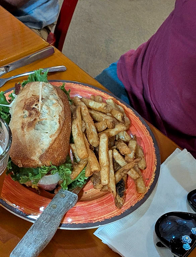 A hearty sandwich served with golden fries &ndash; the perfect fuel for waterfall adventures, presented on a rustic orange plate that pops with color.