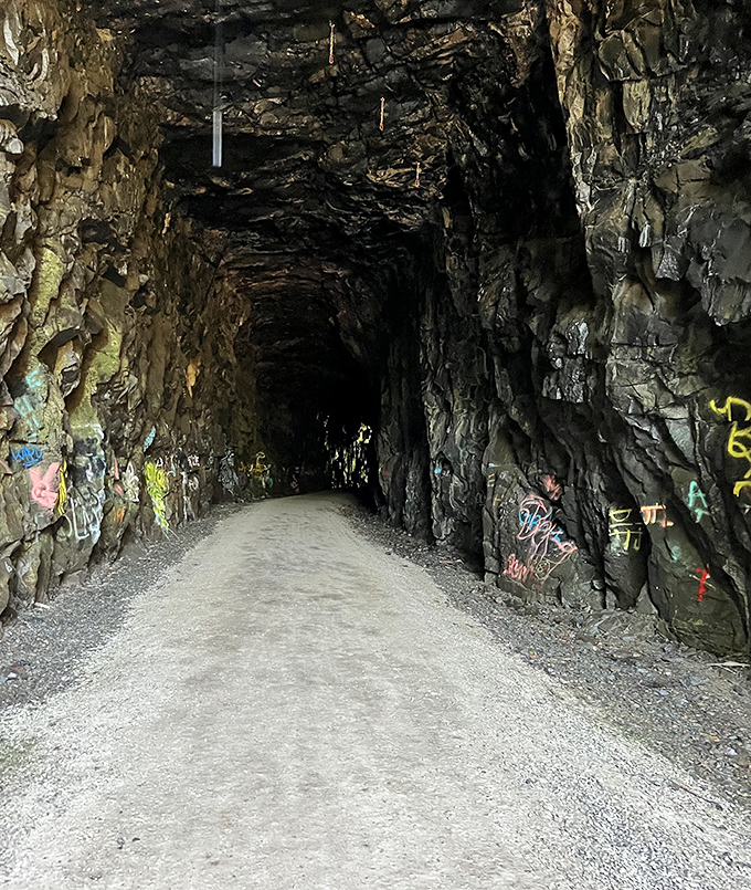 Graffiti meets geology: The tunnel's entrance shows the collision of human expression and ancient rock, urban art in a wilderness setting.