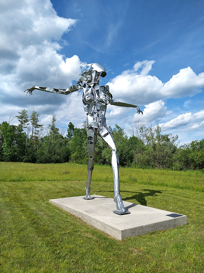 This metallic figure stretches toward the Vermont sky, its reflective surface mirroring clouds and trees in an ever-changing display.