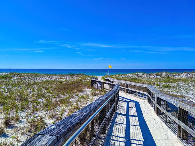 A wooden boardwalk stretches toward the horizon, inviting visitors to cross pristine dunes to discover the Gulf's emerald waters beyond.