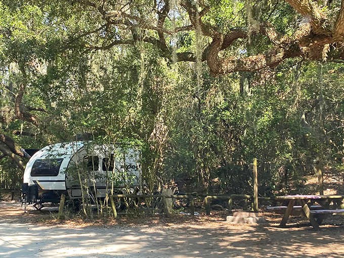 A travel trailer parked at Fort Clinch State Park with tall trees providing shade and the historic fort visible in the distance.