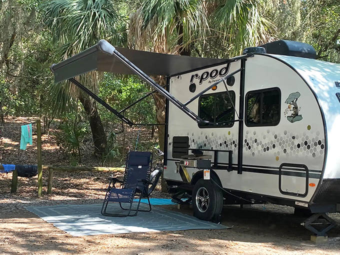A compact camping trailer nestled in the wooded campground at Fort Clinch, showing how the sites blend with the natural environment.
