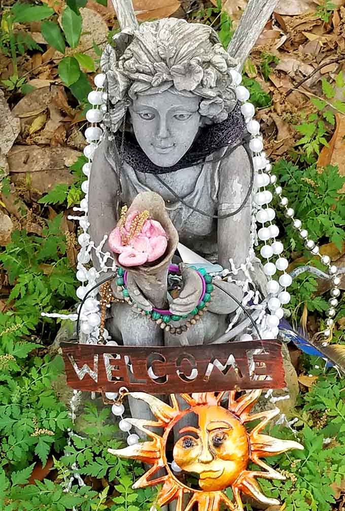 A welcoming garden statue adorned with beads and a cheerful sun reminds visitors that this magical realm operates on a strict policy of good vibes only.