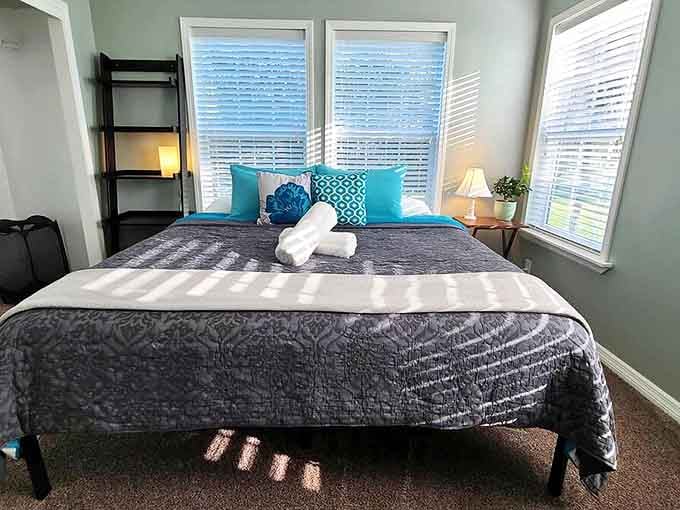 The master bedroom offers cloud-like comfort with its plush bedding and turquoise accents, while natural light pours in from three sides.