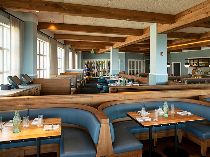 Blue banquettes curve like gentle waves, offering strategic vantage points for both people-watching and gulf-gazing. The wood beams add warmth to balance the cool coastal palette.