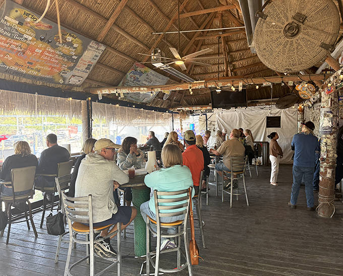 Locals and visitors alike gather under the thatched roof, united by the universal language of fresh seafood and cold drinks.