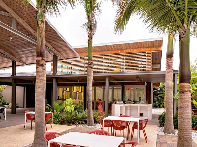 Red chairs pop against lush greenery, creating outdoor dining spaces that feel like secret garden rooms designed for intimate conversations.