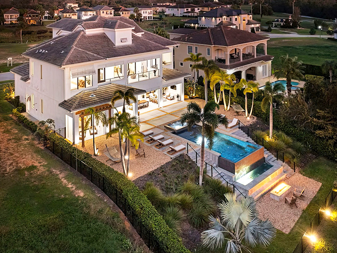 Architectural beauty revealed from above as this white mansion nestles among palms with its geometric pool creating a backyard oasis.