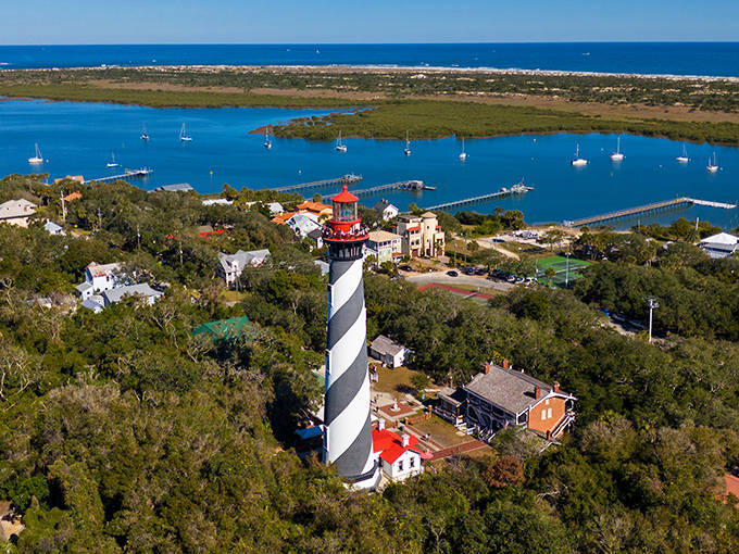 Aerial view of the St. Augustine Lighthouse surrounded by lush greenery, where visitors report hearing phantom footsteps climbing the 219 stairs after dark.