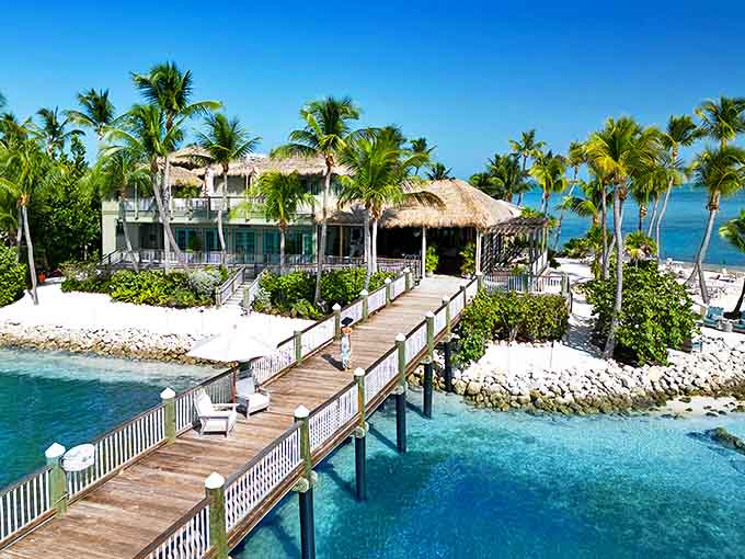 A wooden walkway stretches over turquoise waters to a thatched-roof paradise, promising barefoot luxury on Little Palm Island.