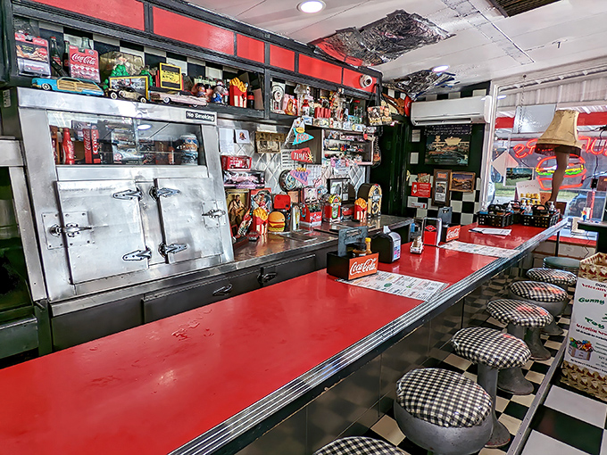 Red countertops gleam beneath vintage memorabilia, creating a time capsule where every Coca-Cola sign tells a story and every stool holds memories.
