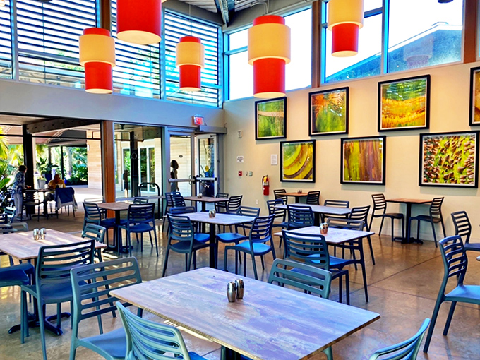 Bright pendant lights dangle like exotic fruits above the airy interior, where colorful artwork and blue chairs create a cheerful tropical vibe.