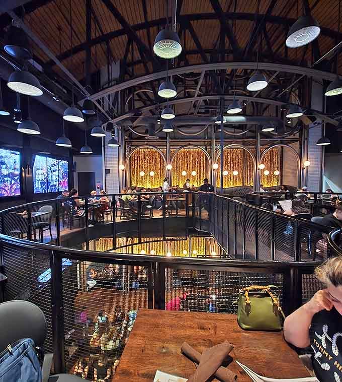 Two-story industrial-chic dining space where brass railings and warm lighting create an intimate atmosphere despite the grand scale&mdash;Jules Verne would approve.