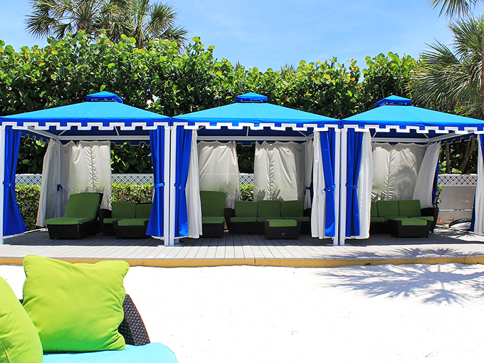 Private beach cabanas stand like blue-and-white sentinels of relaxation, offering shade and style for those serious about their lounging game.