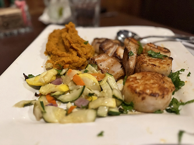 Perfectly seared scallops share the spotlight with fresh vegetables in a plate that celebrates simplicity and quality over flashy presentation.