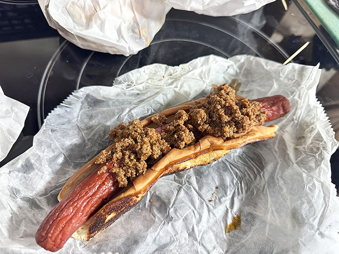 The footlong hot dog stretches beyond its bun like a delicious dare, topped with hearty chili that transforms lunch into an adventure.