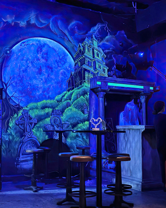 The haunted mansion aesthetic comes alive with this eerie blue lighting illuminating a spooky house mural against a stormy backdrop.