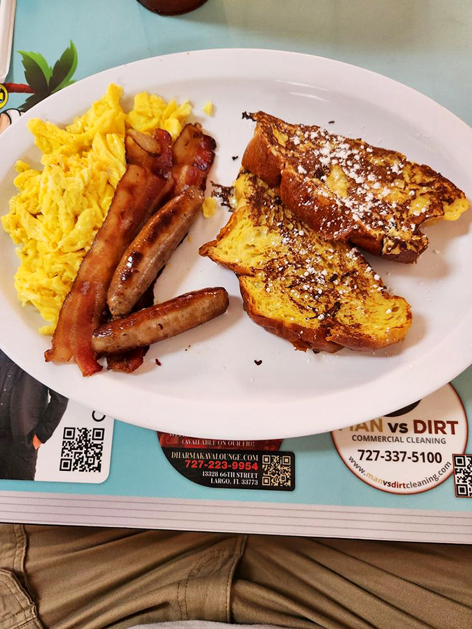 The classic breakfast trinity: perfectly scrambled eggs, crispy bacon, and French toast dusted with powdered sugar &ndash; simple perfection on a plate.