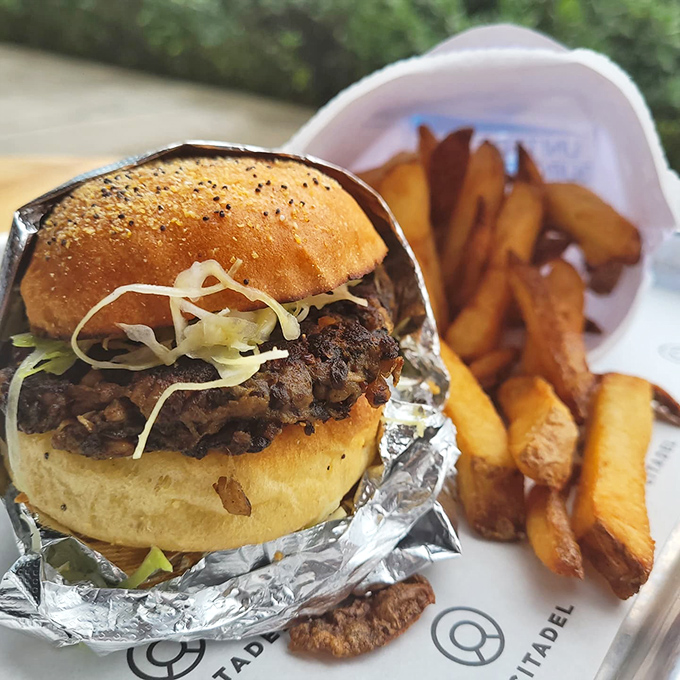 The Snail Mail Burger arrives wrapped like a precious package, accompanied by golden fries that deserve their own zip code in Delicious Town.