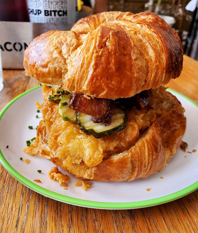 Breakfast architecture at its finest: a buttery croissant sandwich stacked with crispy chicken, bacon, and fresh ingredients.