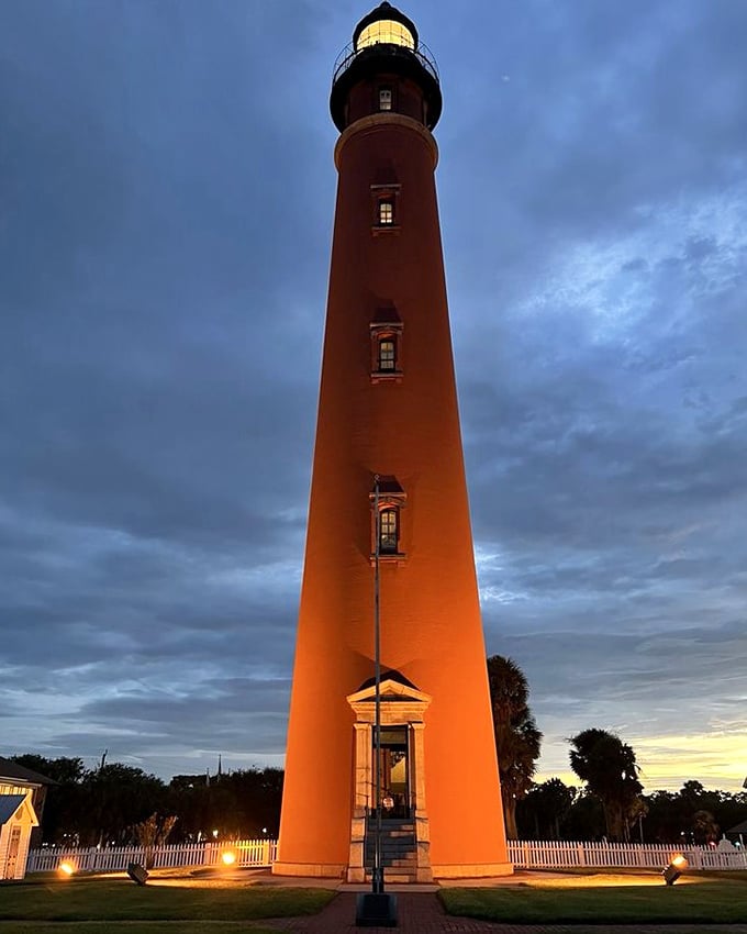 As twilight descends, the illuminated lighthouse transforms from daytime sentinel to nocturnal guardian, its warm glow visible for miles across the water.