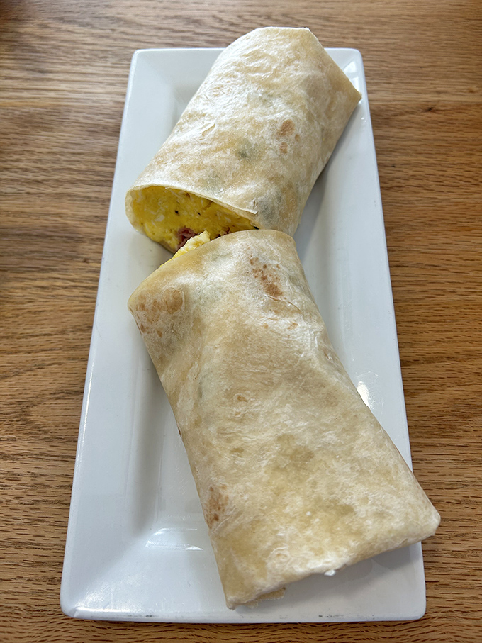 A neatly wrapped breakfast burrito, cut to reveal a treasure trove of morning goodness inside the warm tortilla.
