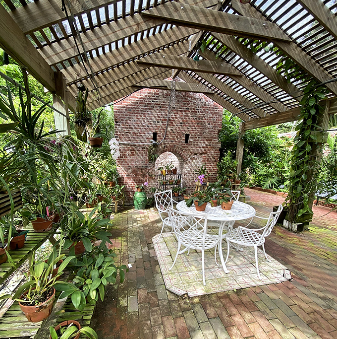 Dappled sunlight plays across this garden patio, where white furniture pops against weathered brick and lush greenery.