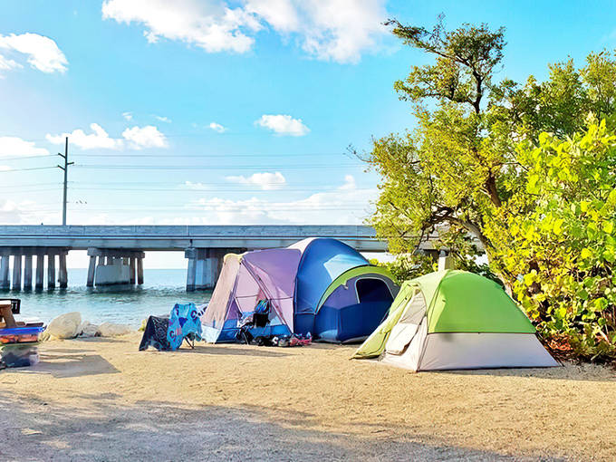 A camping tent set up near Bahia Honda's shoreline, with the historic bridge visible in the background under dramatic skies.
