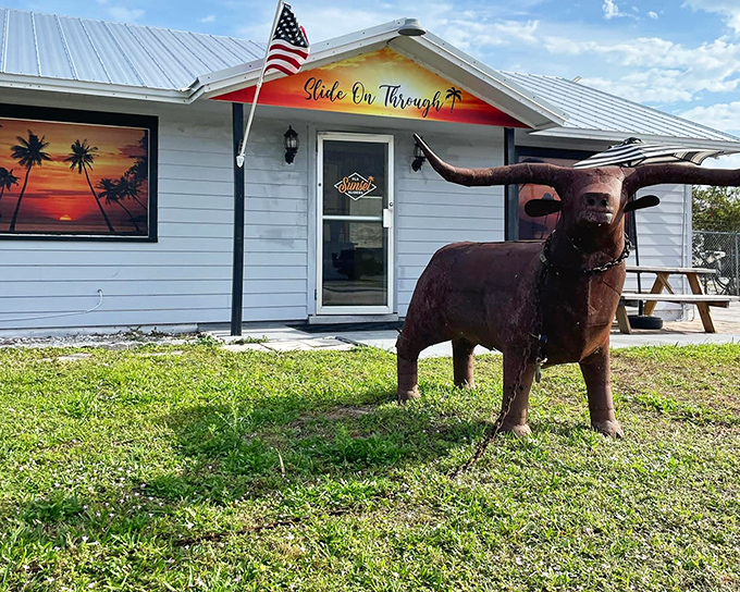 The longhorn sentinel stands guard outside this unassuming treasure, where the "Slide On Through" sign promises delicious adventures await inside.
