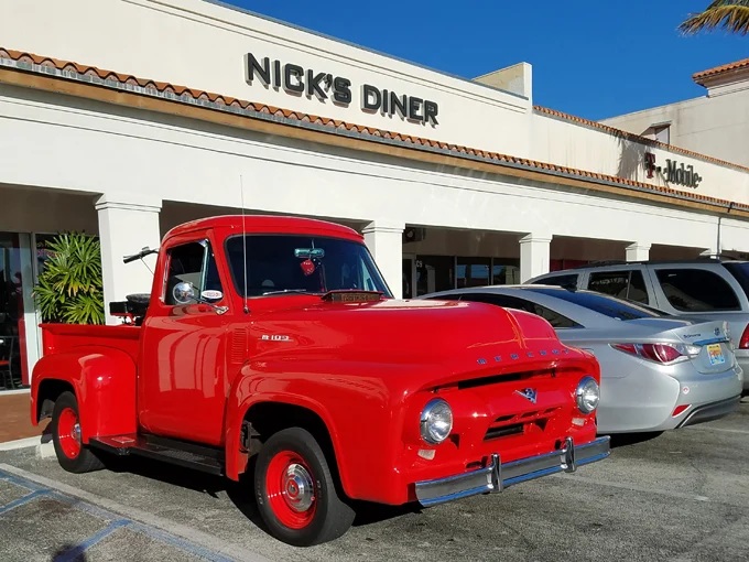 The classic cherry-red Ford pickup parked outside Nick's Diner serves as both vintage eye candy and a perfect ambassador for the timeless Americana waiting inside.