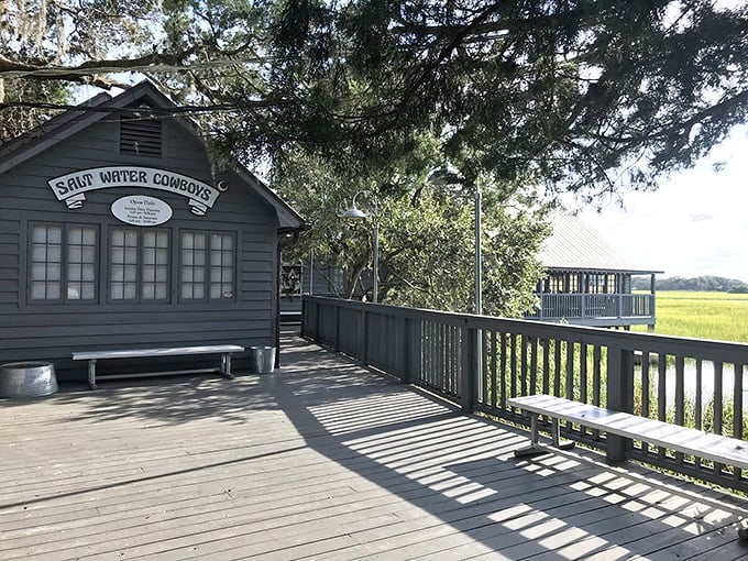 The weathered gray exterior of Saltwater Cowboys stands sentinel over the marshlands, promising authentic coastal charm before you even step inside.