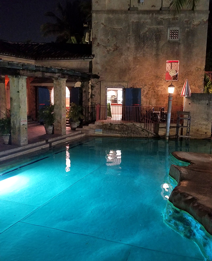 As darkness falls, the pool transforms into a luminous lagoon, its waters glowing like liquid sapphire against weathered stone.